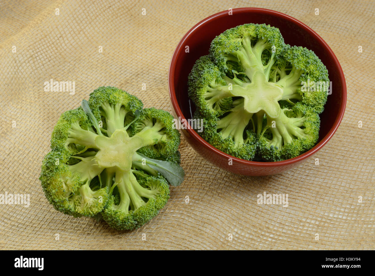 Two heads of broccoli, one inside and one outside of red bowl Stock ...