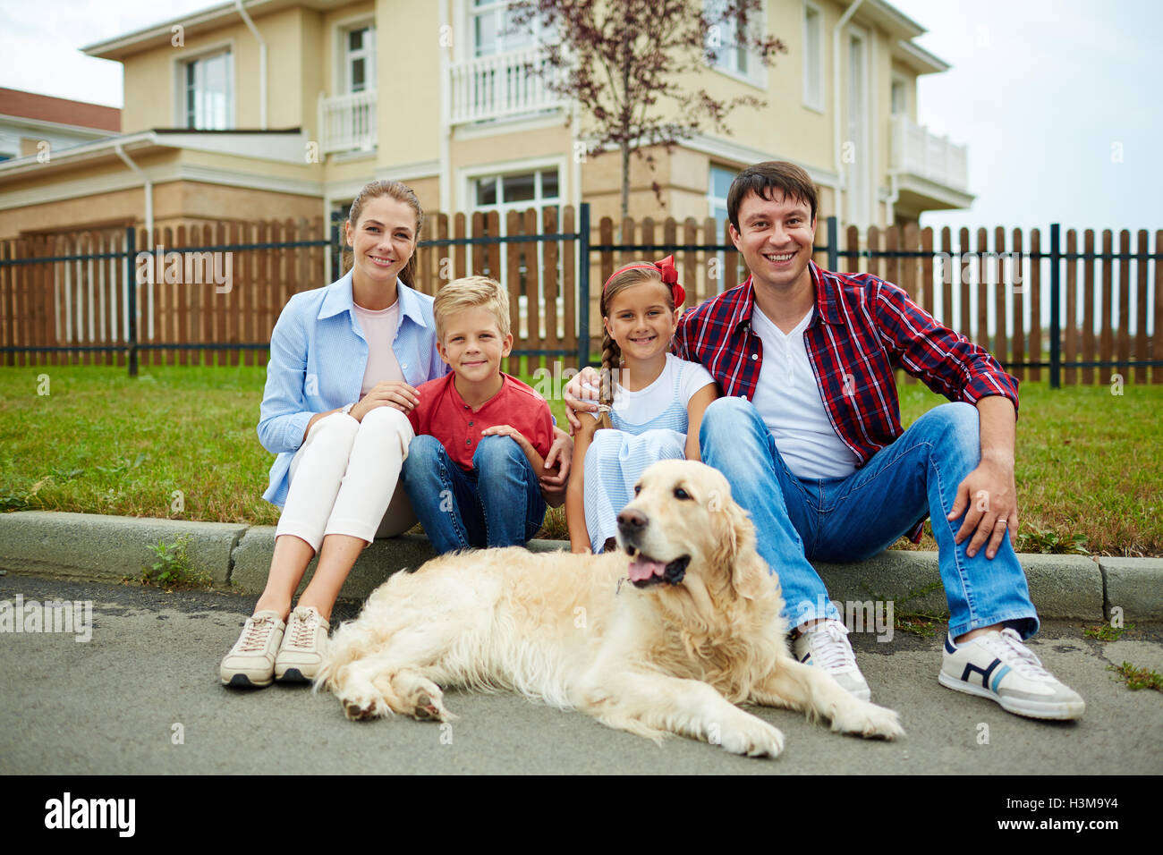 Family of four and their pet sitting by their new house Stock Photo - Alamy