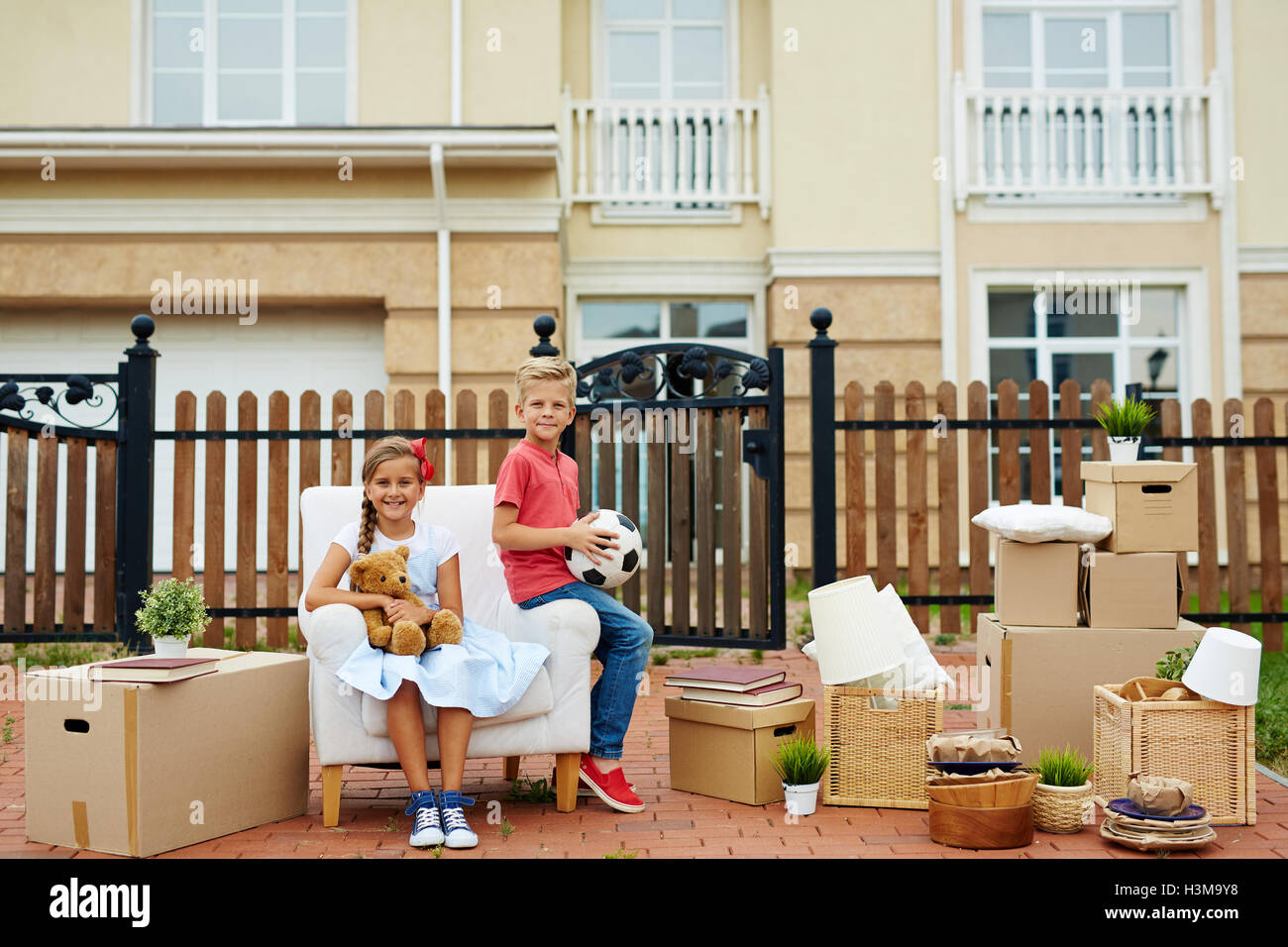 Two kids sitting in armchair in the front yard with packed things near ...