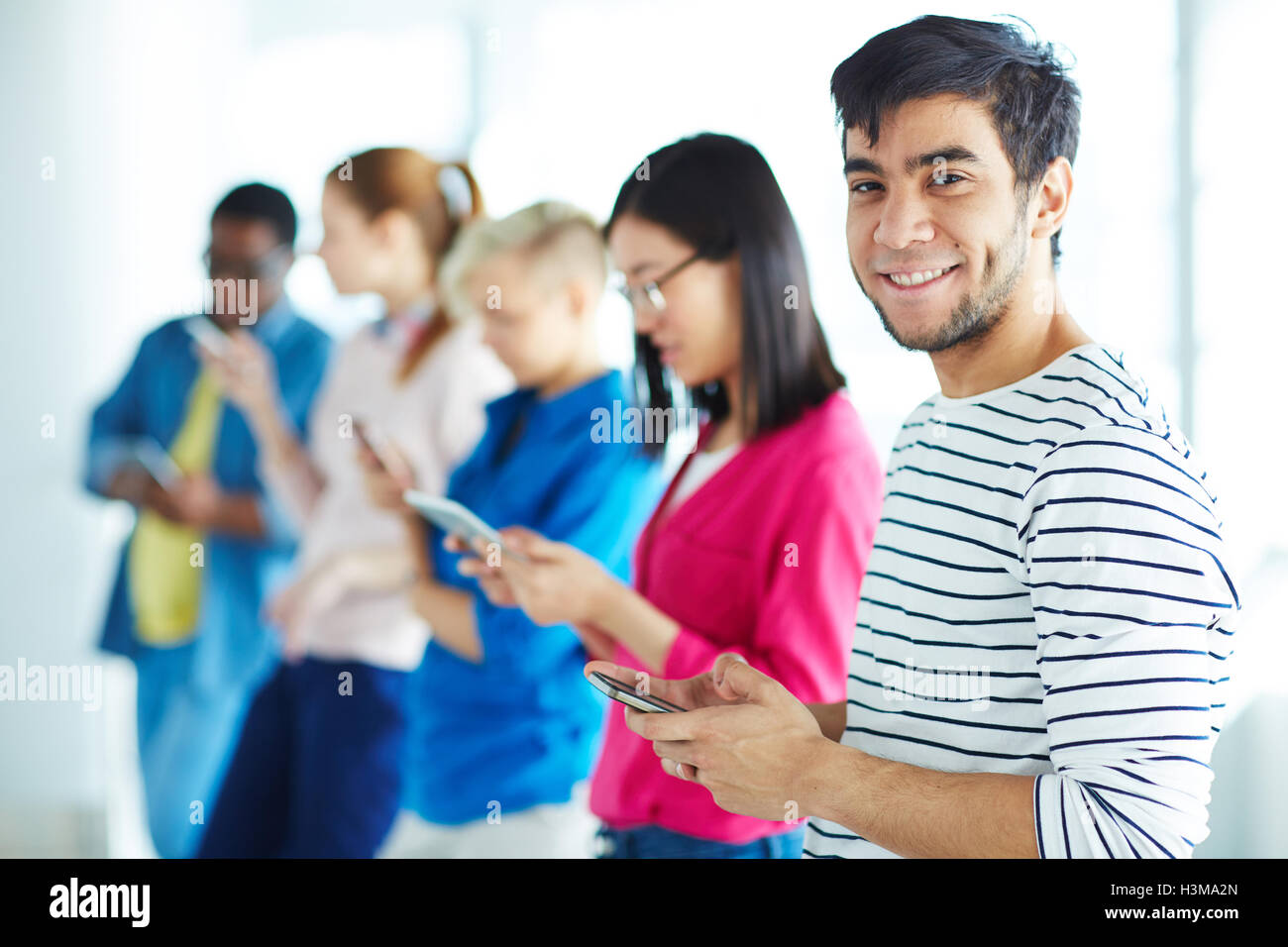 Young guy with cellphone looking at camera with his groupmates on ...