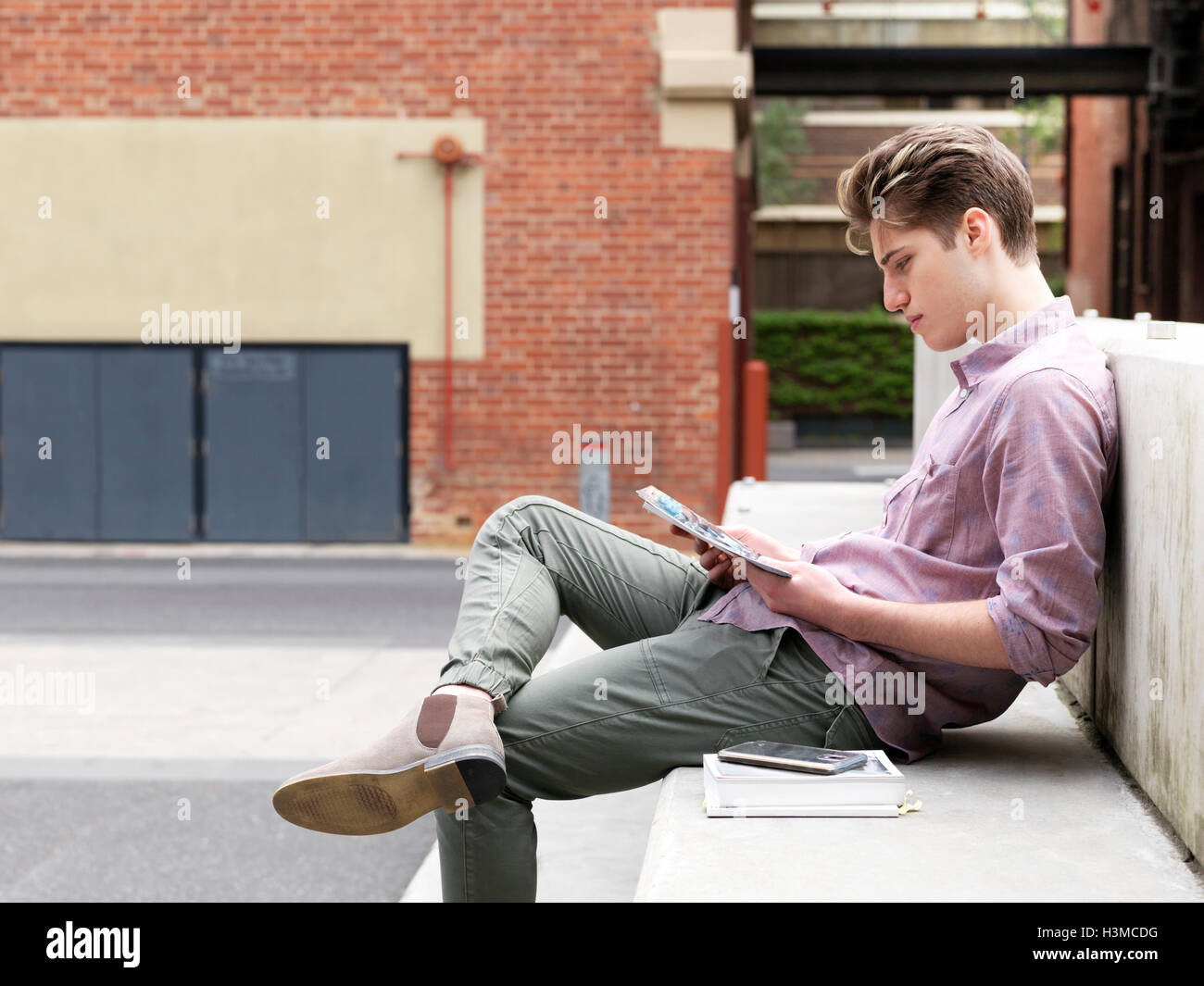 Young man sitting on step, outdoors, reading book Stock Photo - Alamy