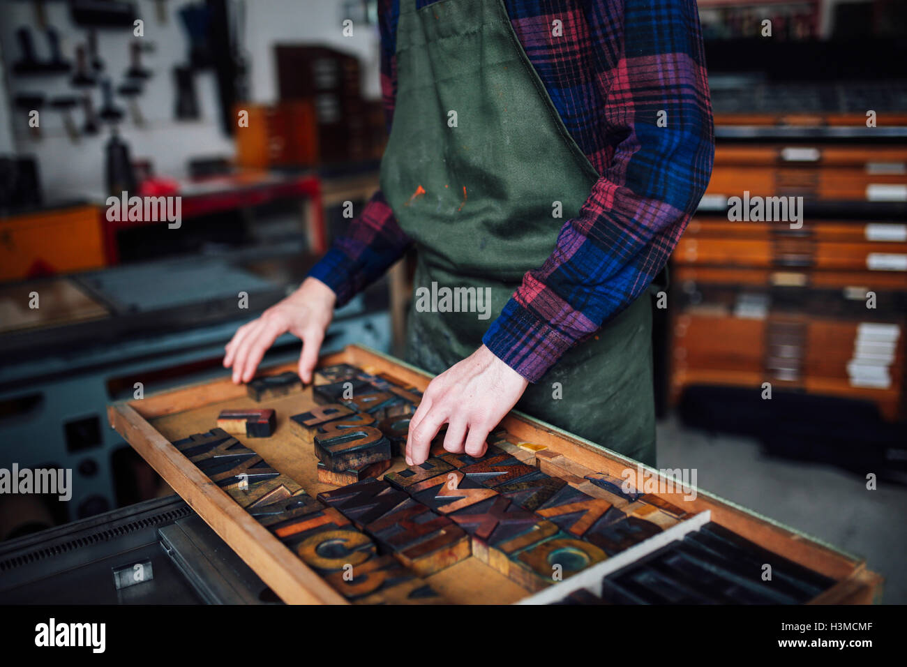 Crop of young craftsman looking through tray of wooden letterpress ...