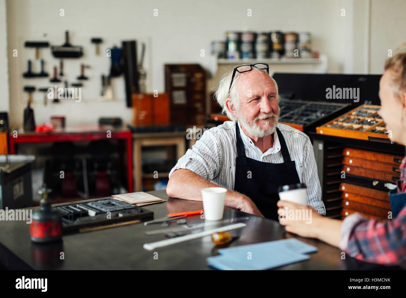 Senior craftsman sitting at table with young craftswoman and smiling in ...