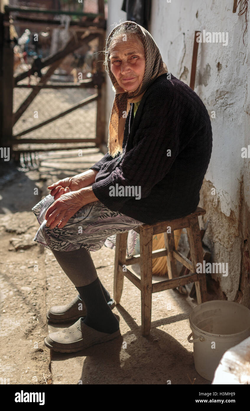 Old woman with kerchief sitting in her backyard in the countryside ...