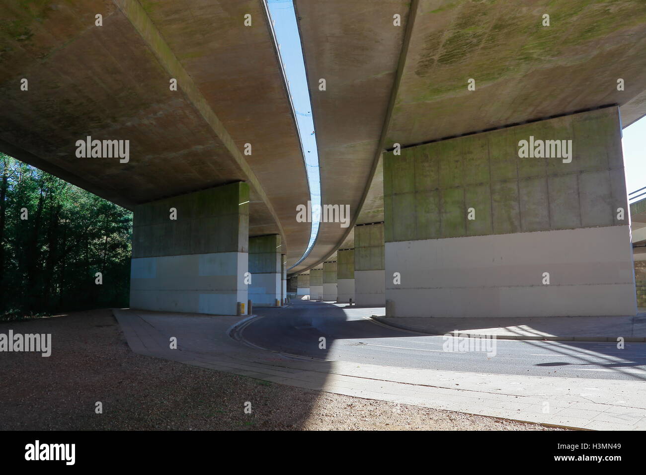 Looking up under the arches of a huge curved concrete flyover with a ...