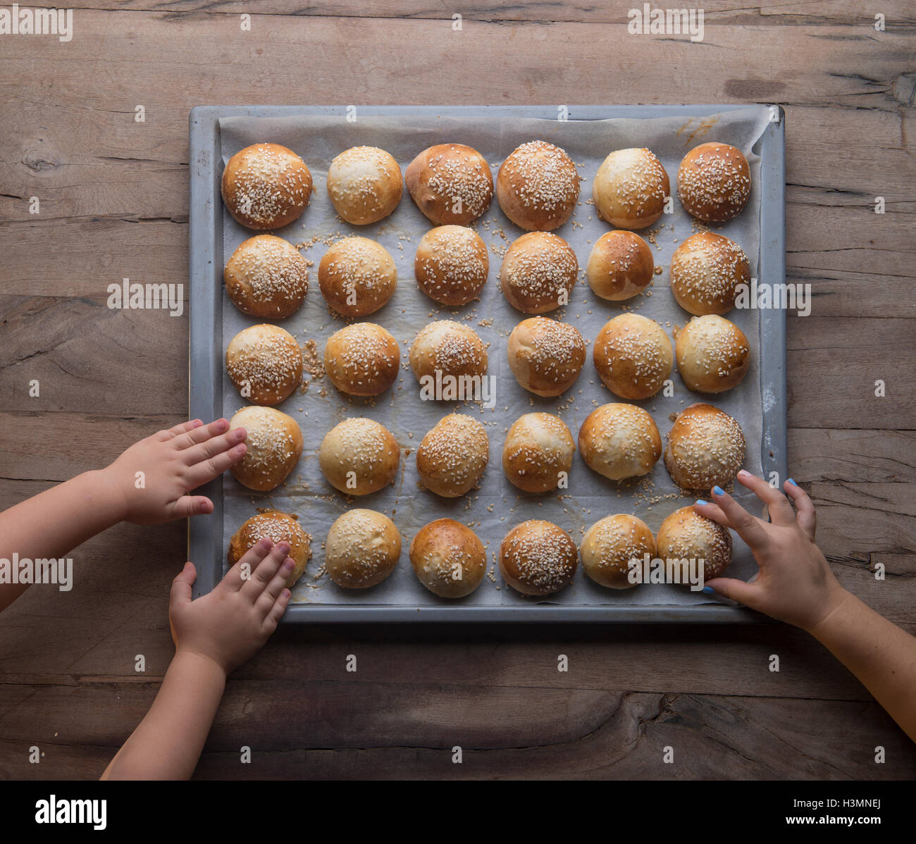 children reaching for fresh baked buns on a tray, wooden table Stock ...