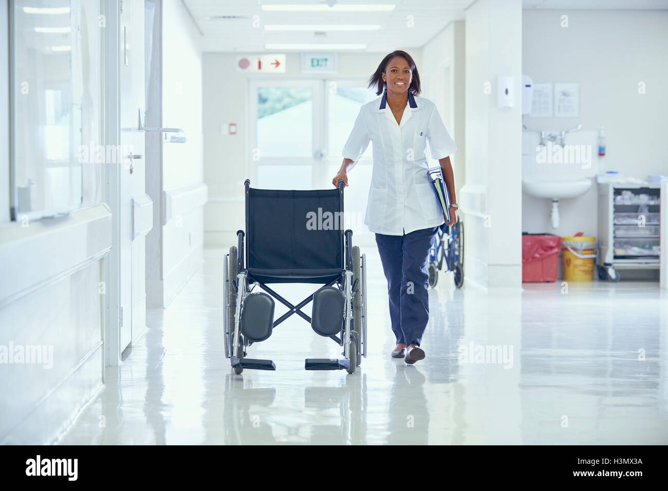 Female orderly pushing wheelchair along hospital corridor Stock Photo ...