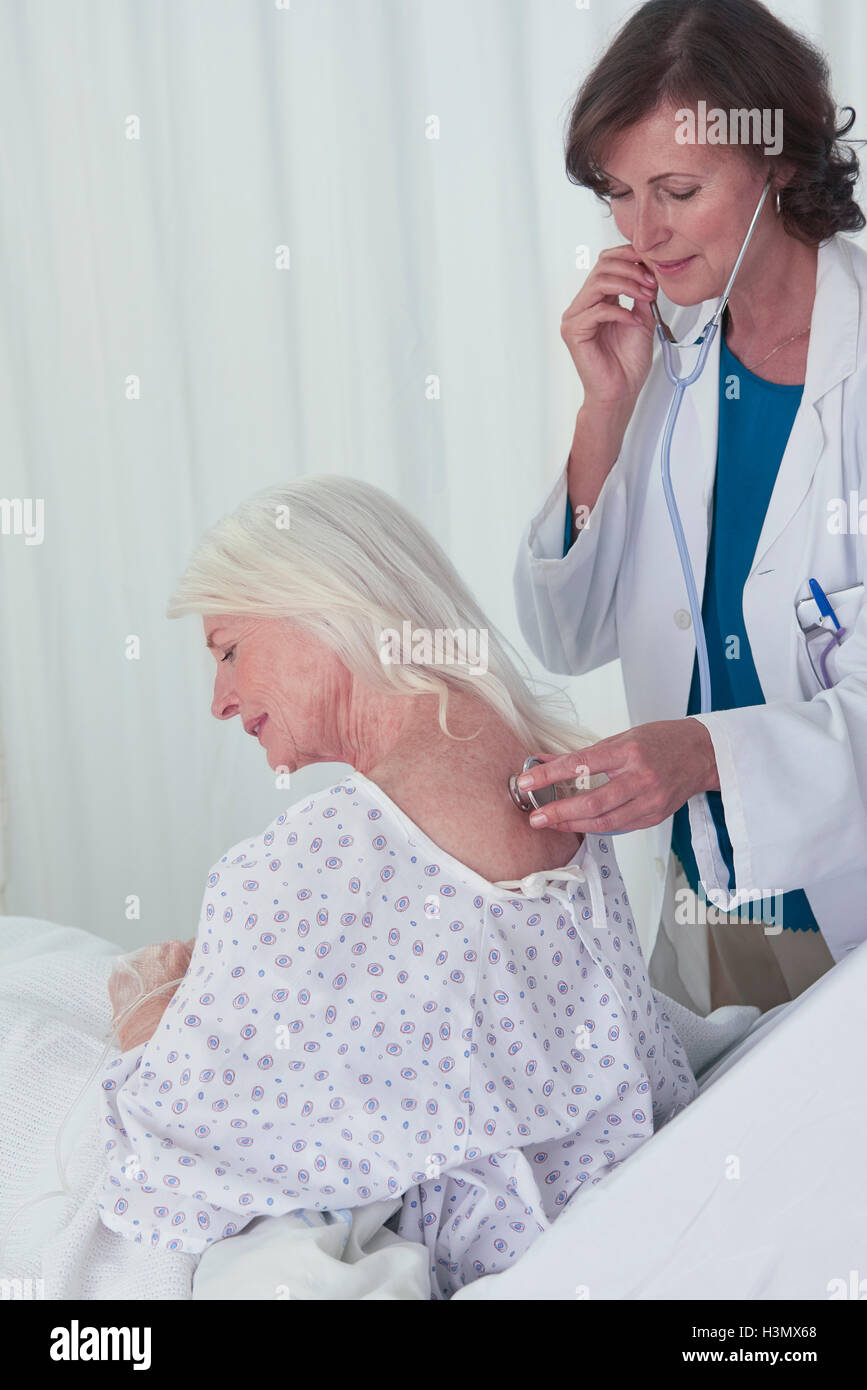 Female doctor listening to senior female patient back with stethoscope ...