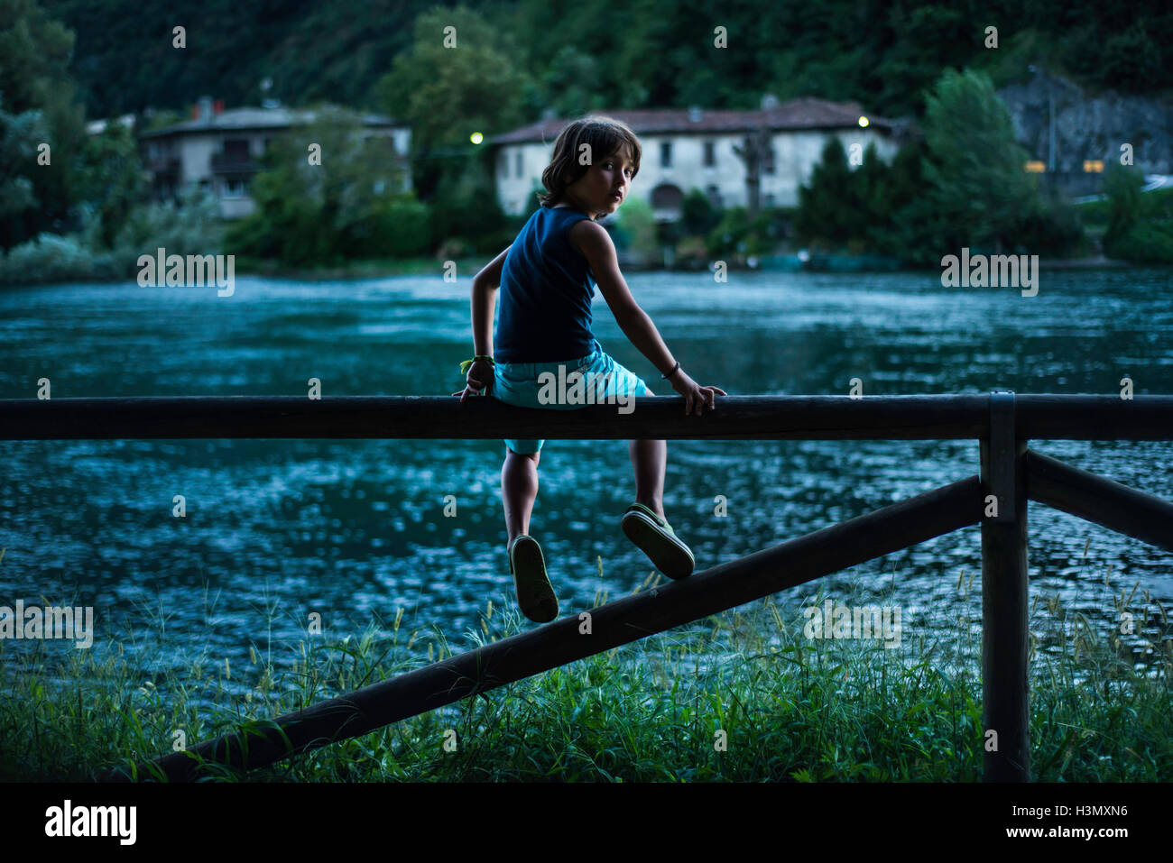 Boy sitting on fence by river looking over shoulder at camera Stock ...
