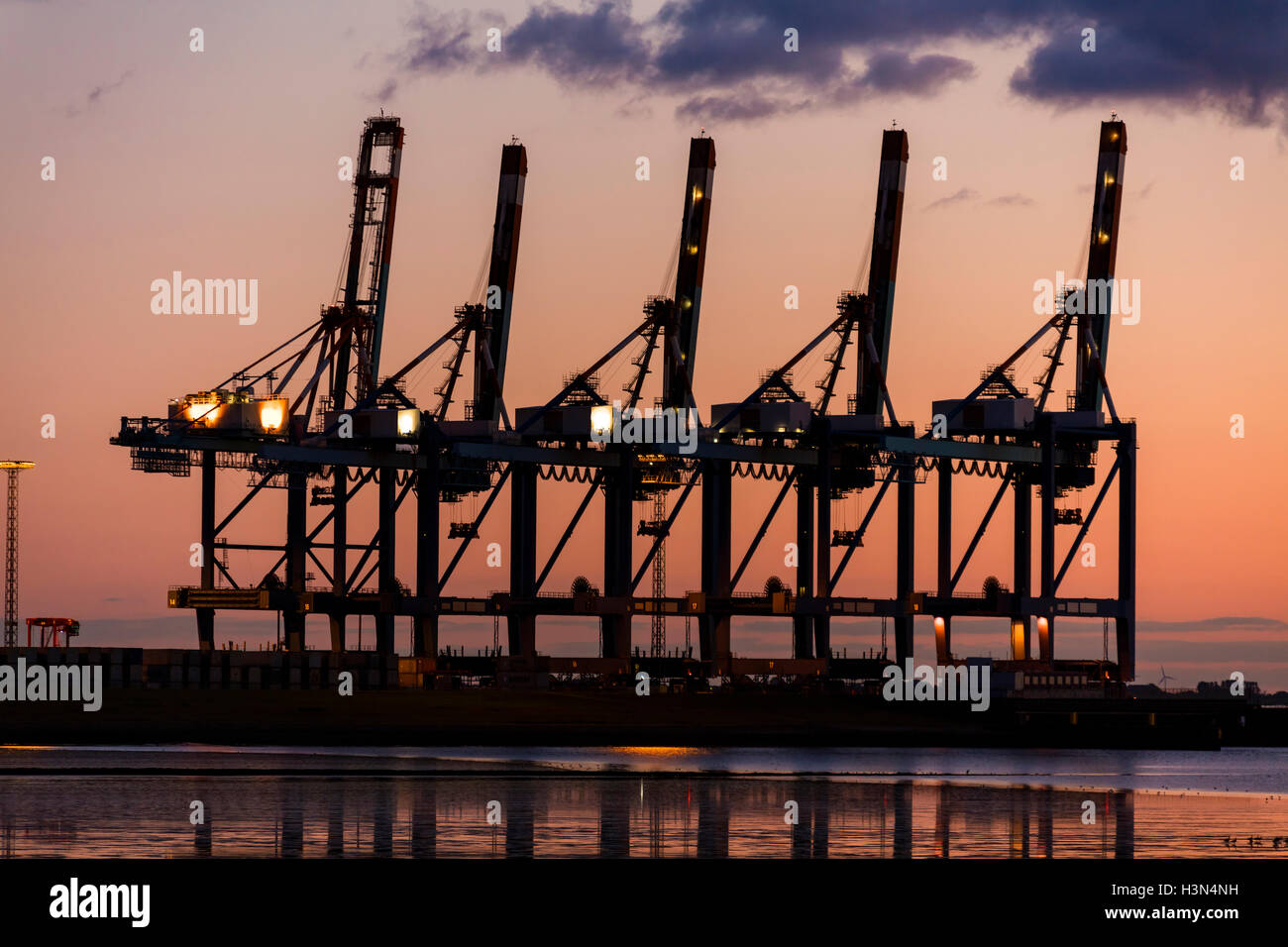 Sunset or sunrise behind cranes at a shipping container port or harbor ...
