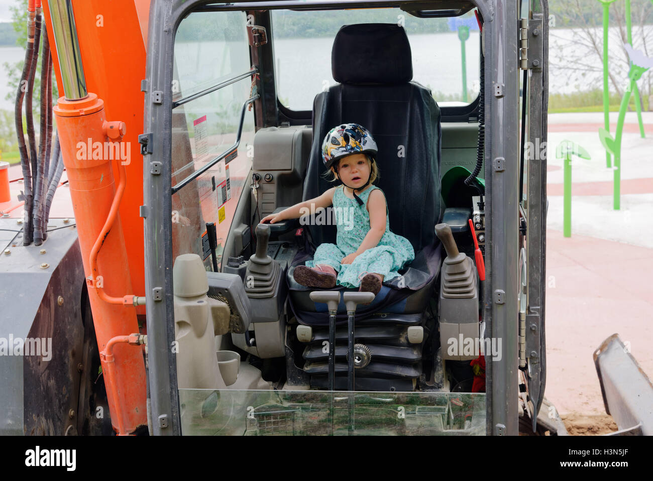 A young girl (2 yrs old) sitting a JCB (excavator) cabin pretending to ...