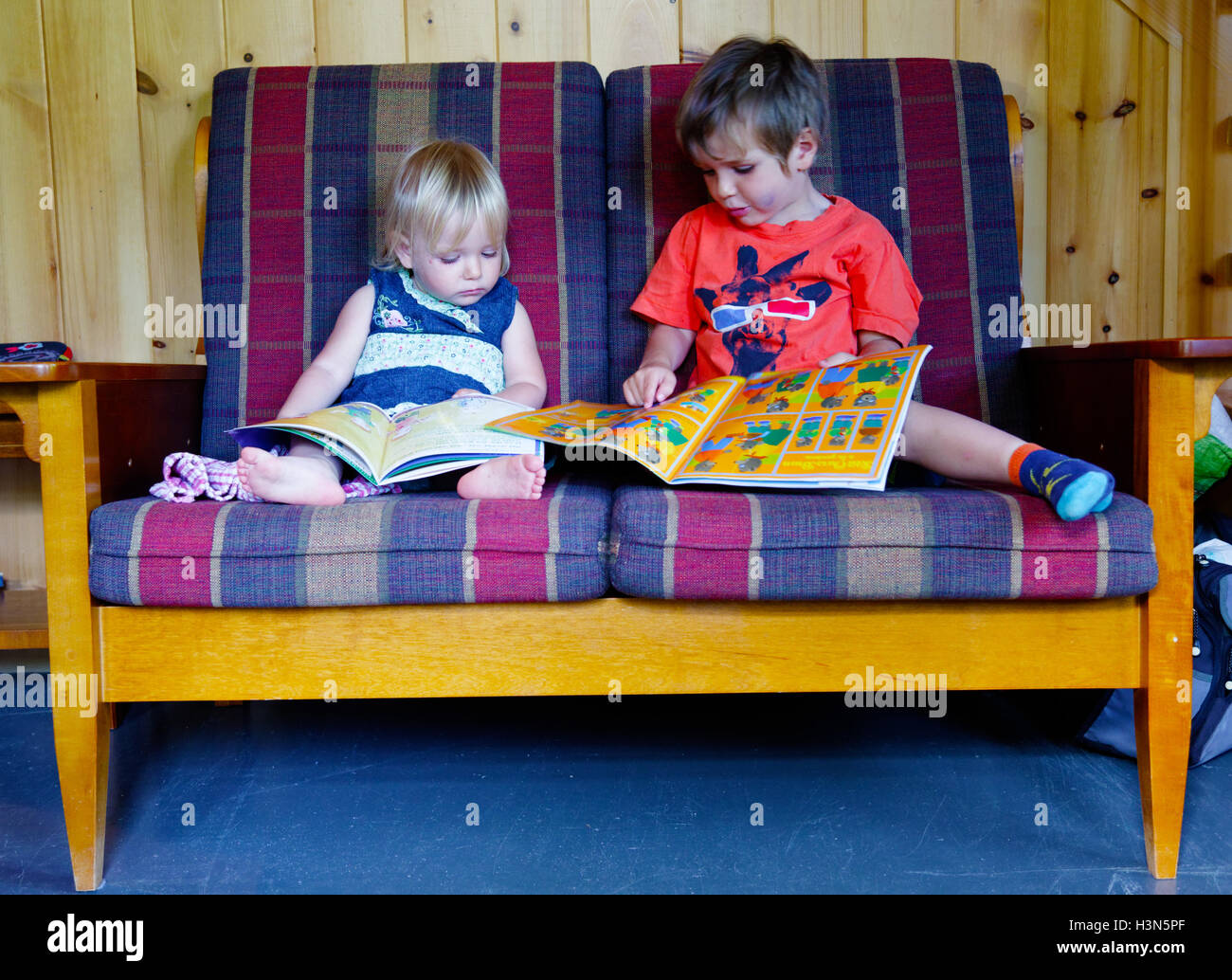 Two young children, brother and sister, sat reading together on a sofa ...