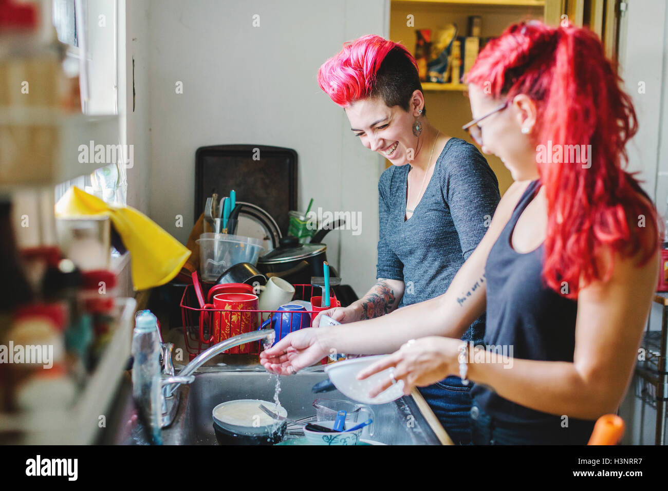 Two young women with pink hair laughing whilst washing dishes at ...