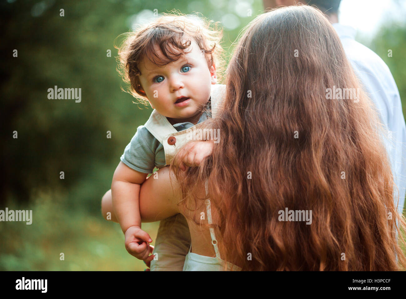 Young beautiful mother hugging her little toddler son against green grass. Happy woman with her ...