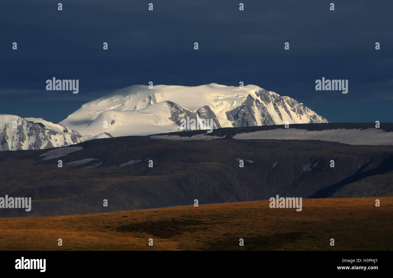 A highland fields with yellow grass on a background of dramatic snow ...
