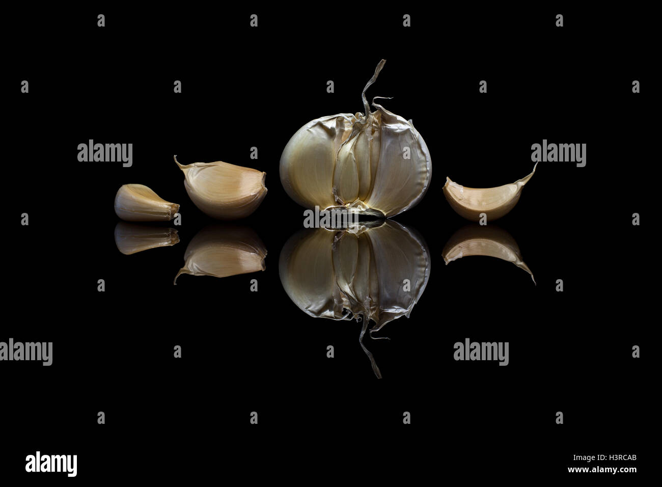 One halved and three peeled garlic isolated on a black reflective ...