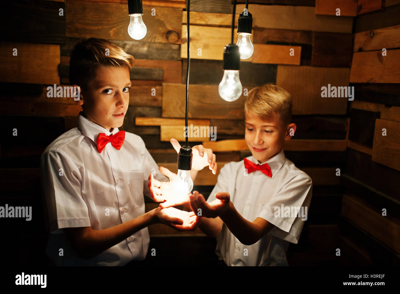 Two brothers posed at studio room wooden wall with enabled light bulbs ...