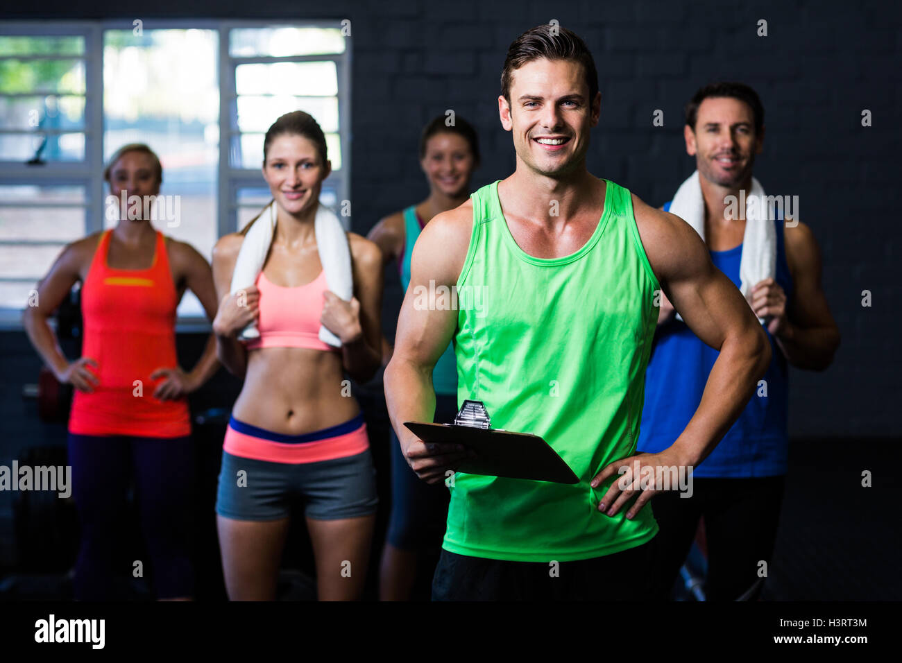Smiling fitness instructor holding clipboard while people standing in ...
