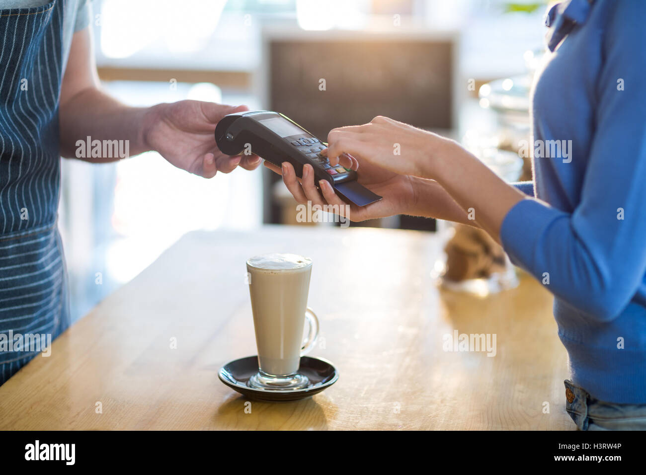 Customer making payment through payment terminal at counter in cafÃ ...