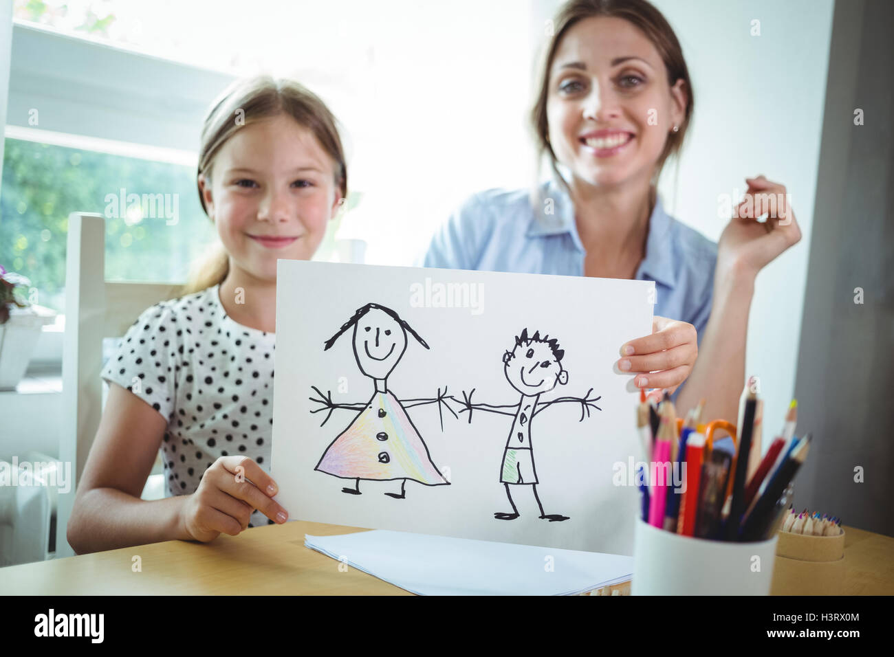 Mother and daughter sitting at table and daughter showing her drawing ...