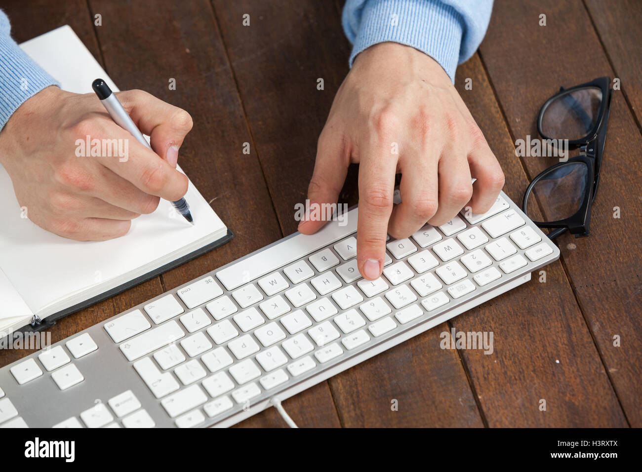Man typing on keyboard and writing in diary Stock Photo - Alamy