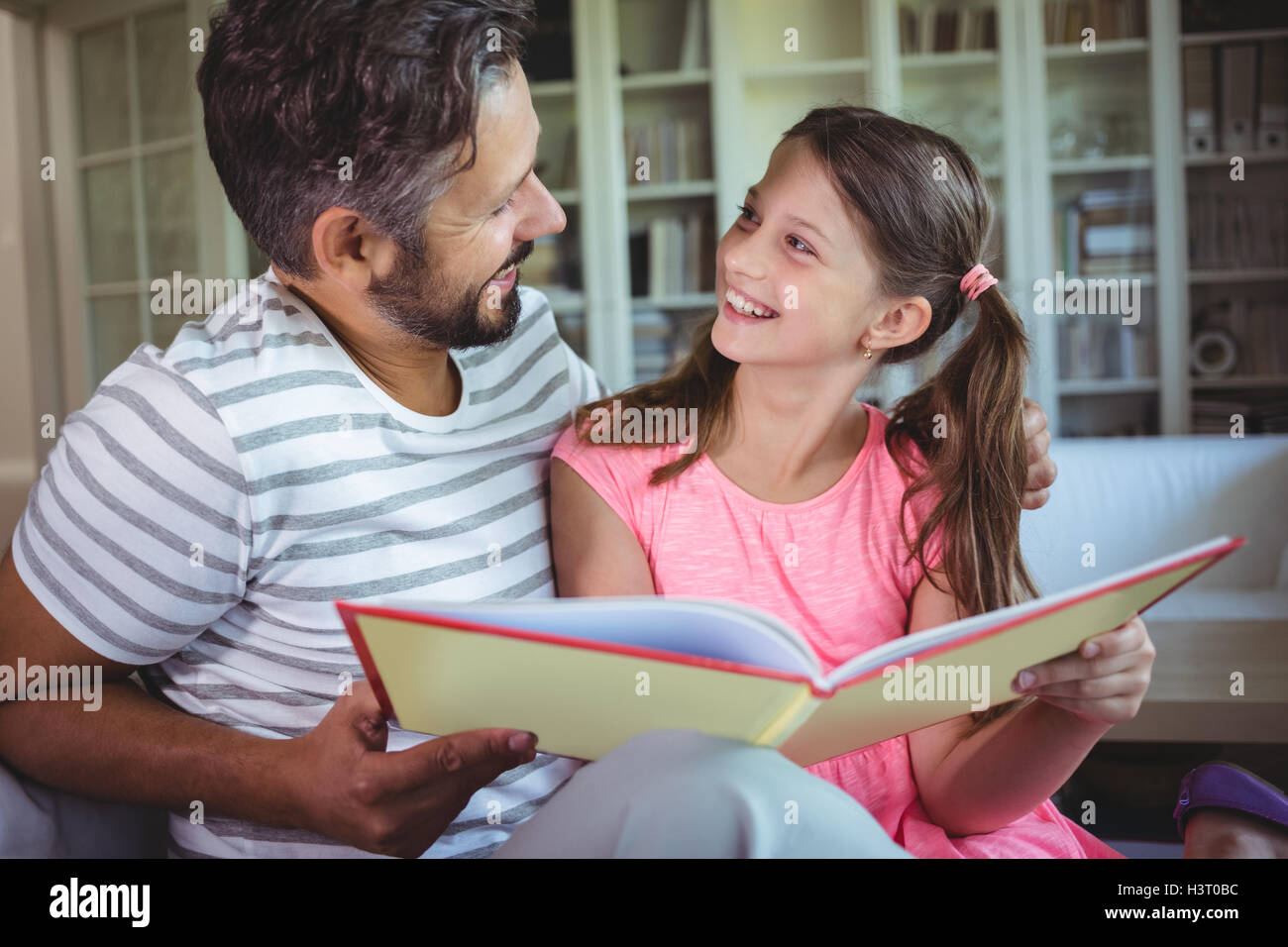 Smiling Father And Daughter Looking At Photo Album In Living Room Stock