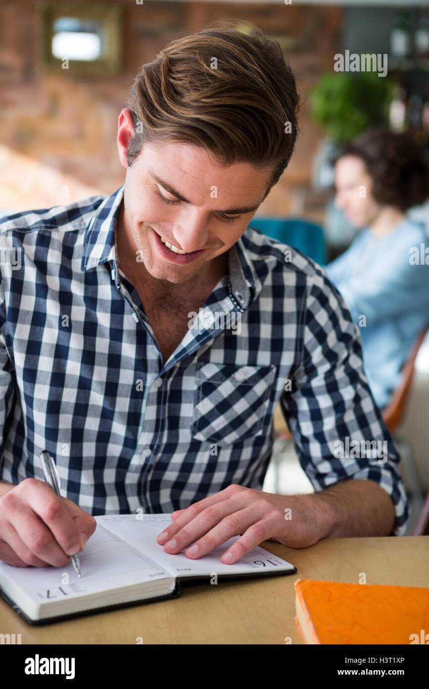 Man writing notes in diary in coffee shop Stock Photo - Alamy