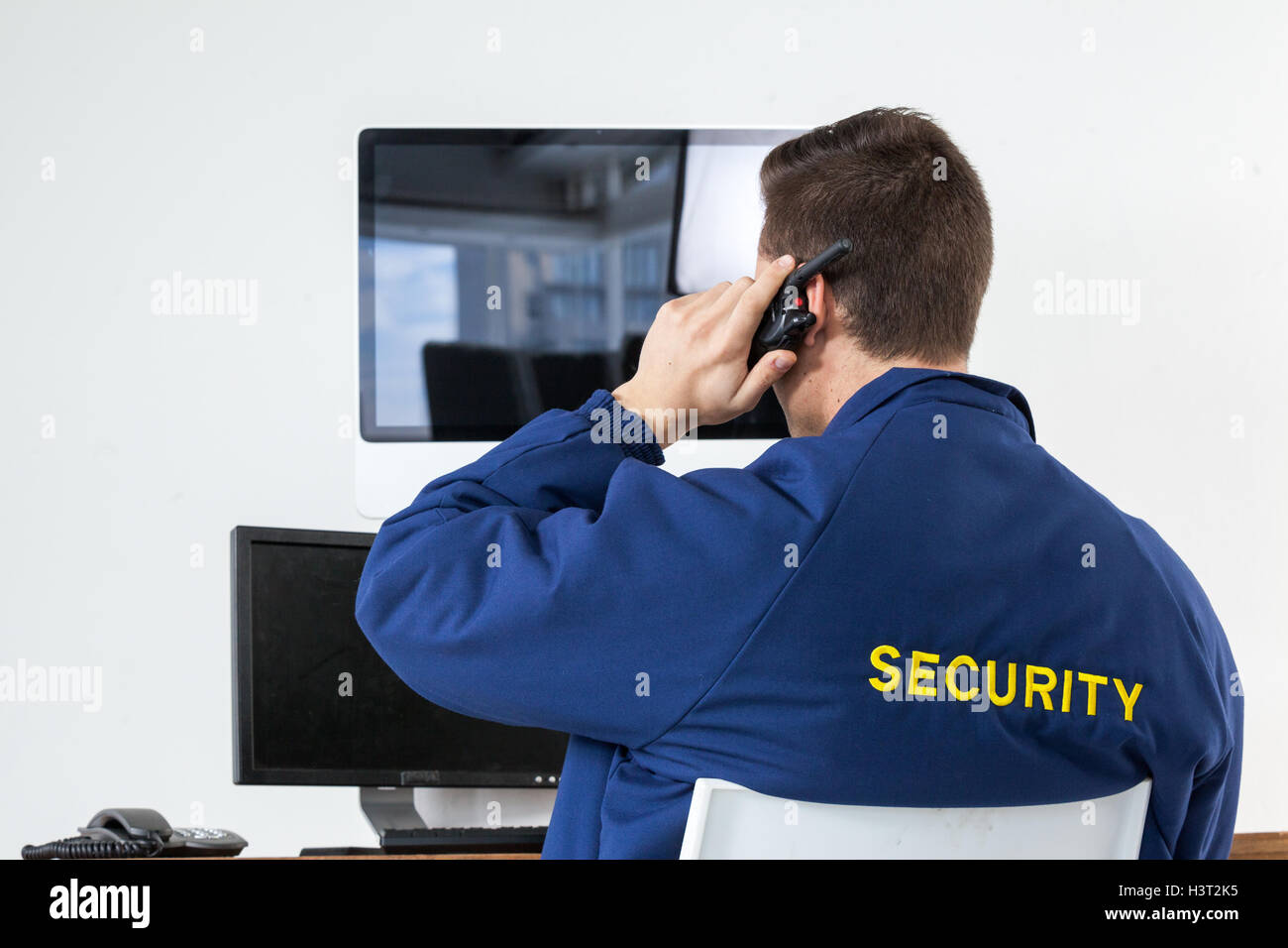 Rear view of security officer talking on walkie-talkie while looking at ...