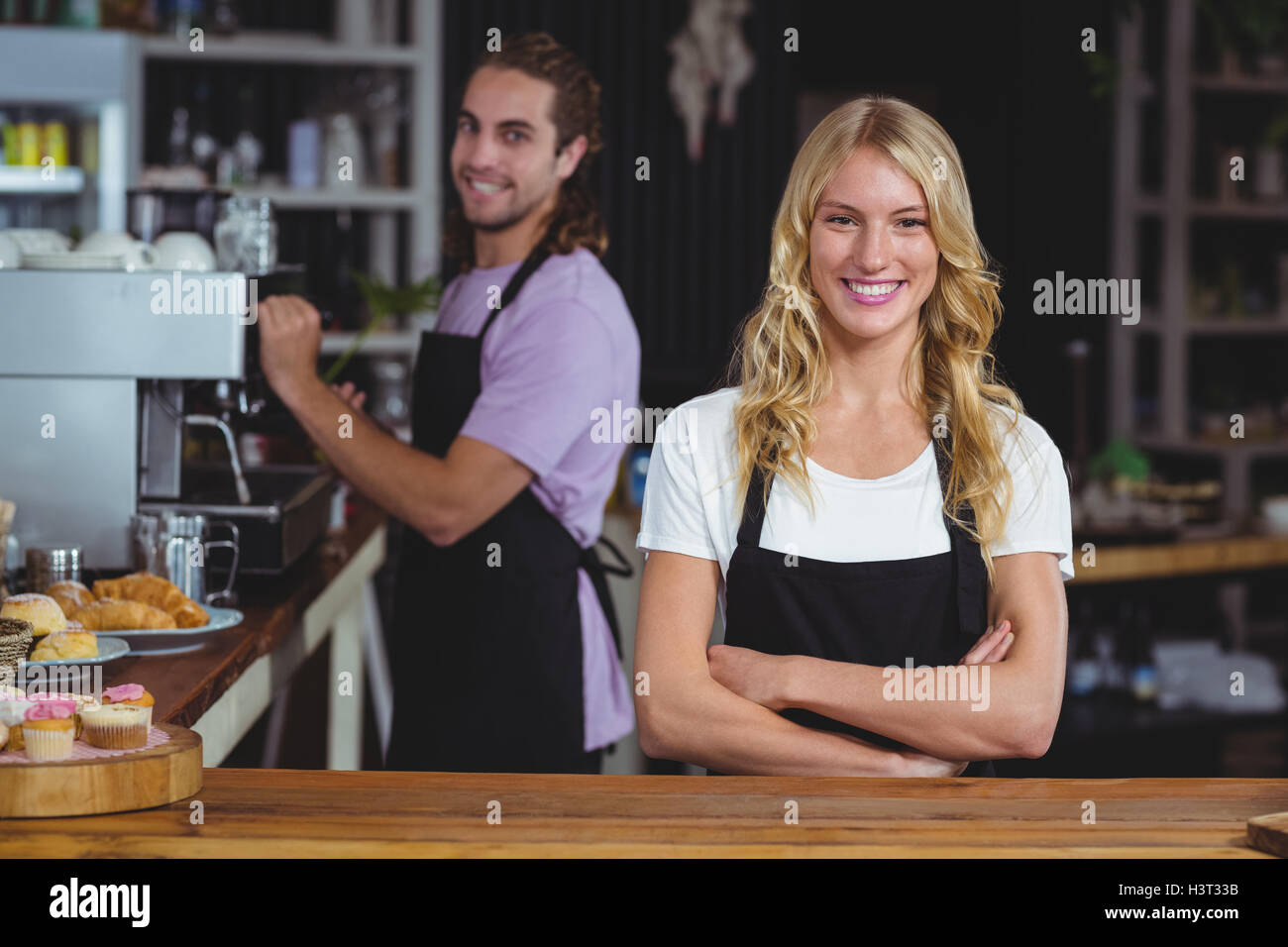 Portrait of smiling waitress standing with arms crossed at counter ...
