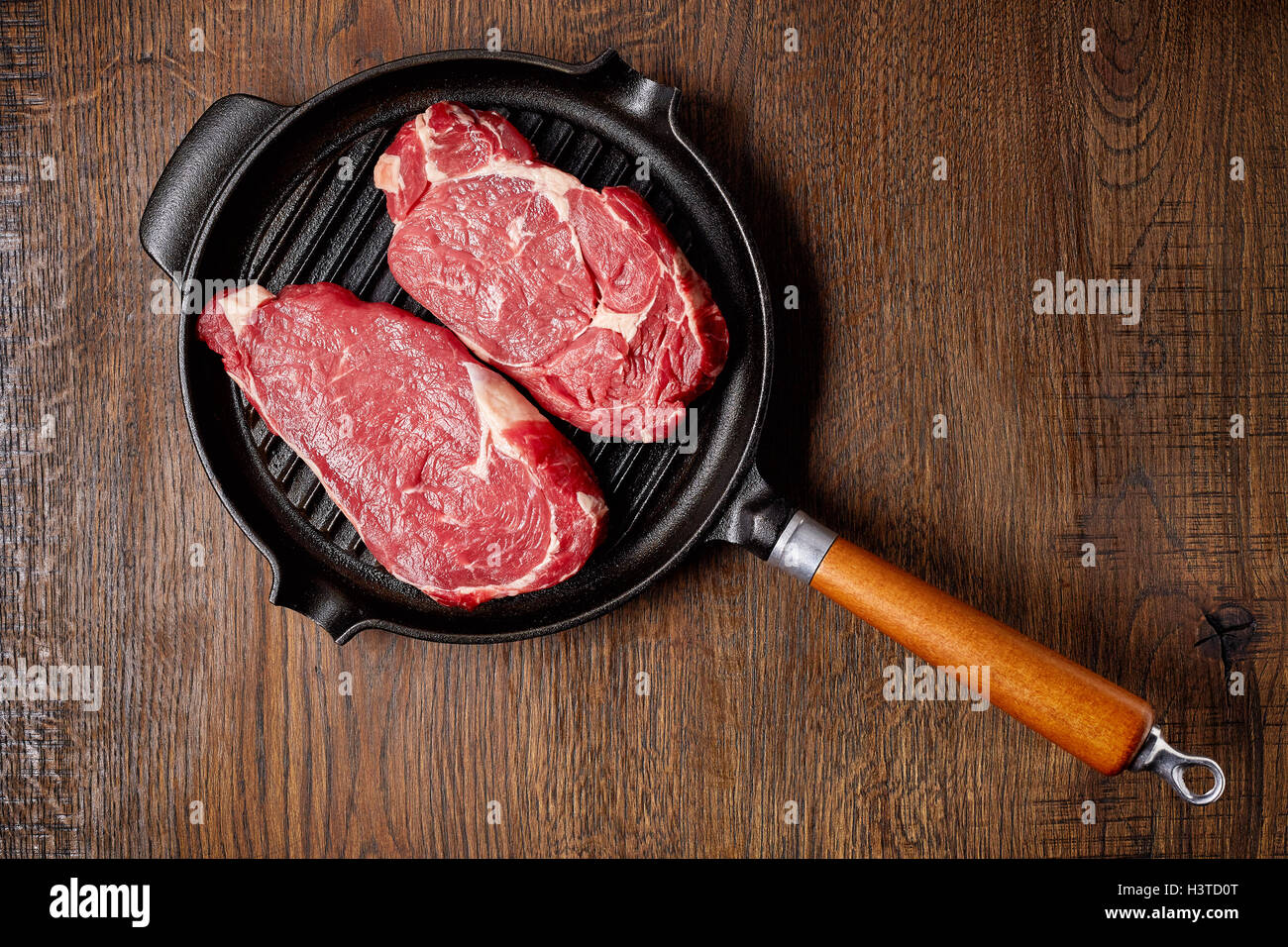 Raw beef steak on grill pan, on wooden table, top view Stock Photo - Alamy