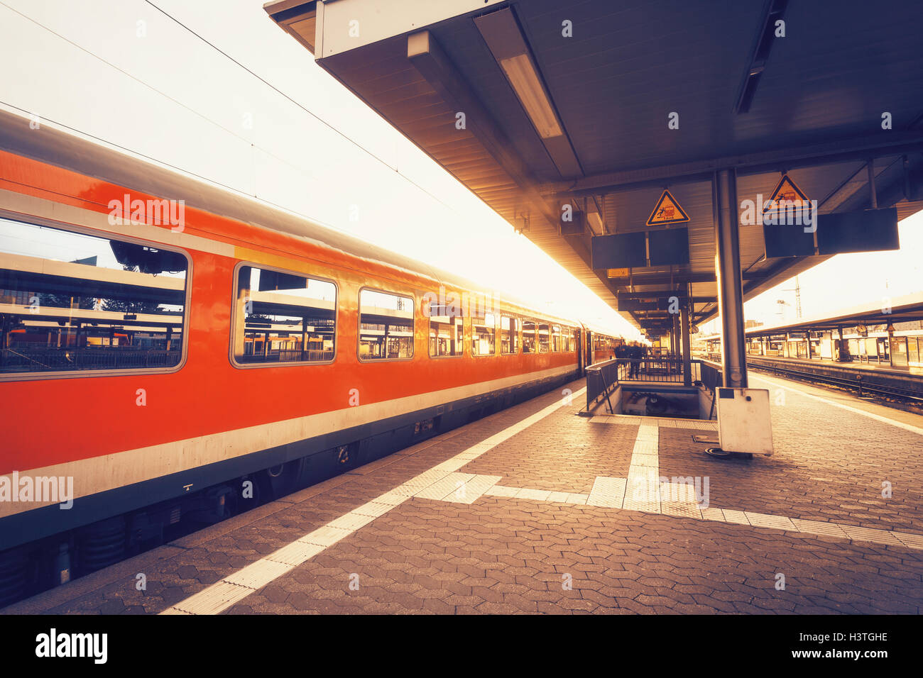 High speed red train at railway platform at sunset. Railway station ...