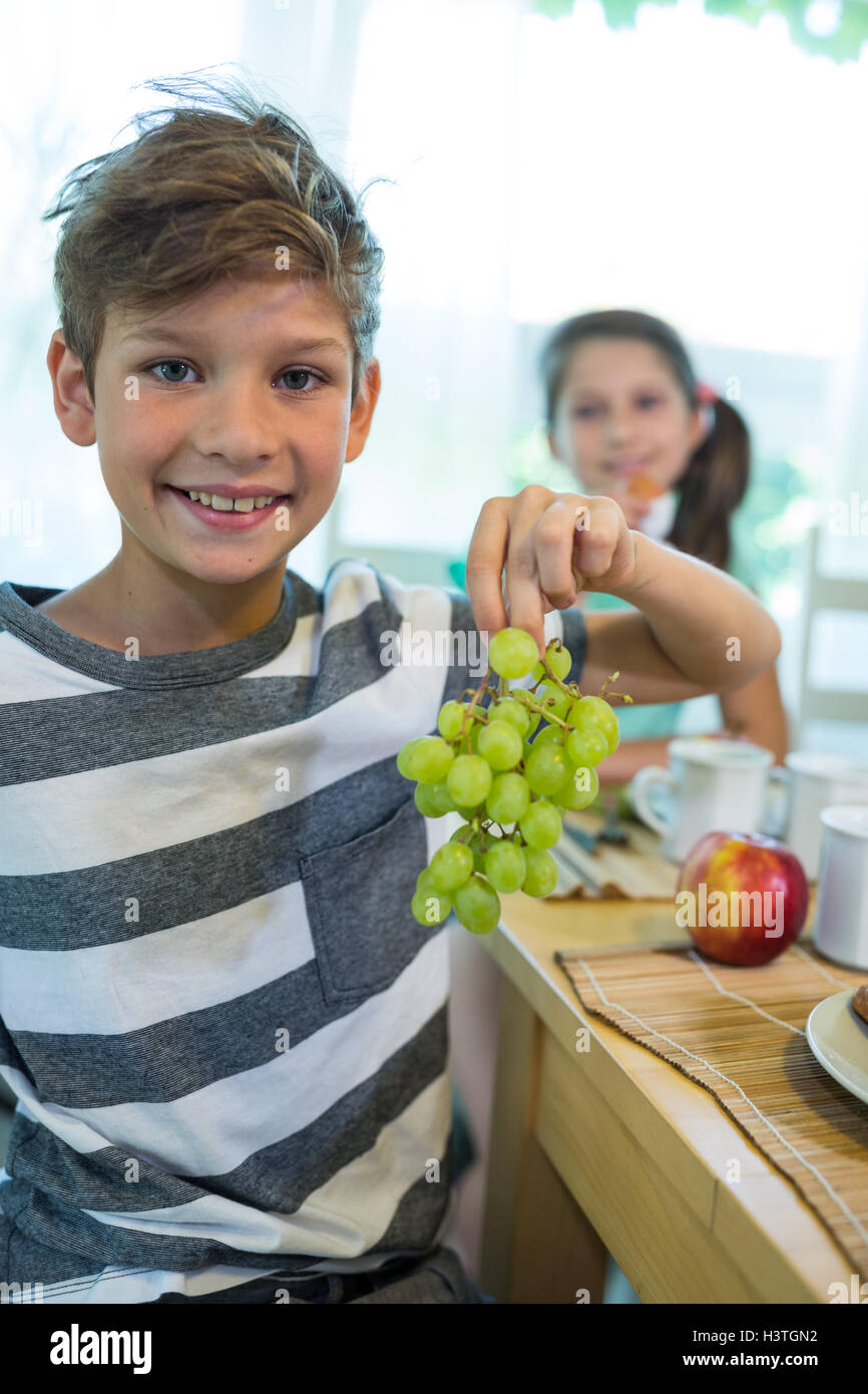 Boy holding a bunch of grapes while having breakfast Stock Photo - Alamy