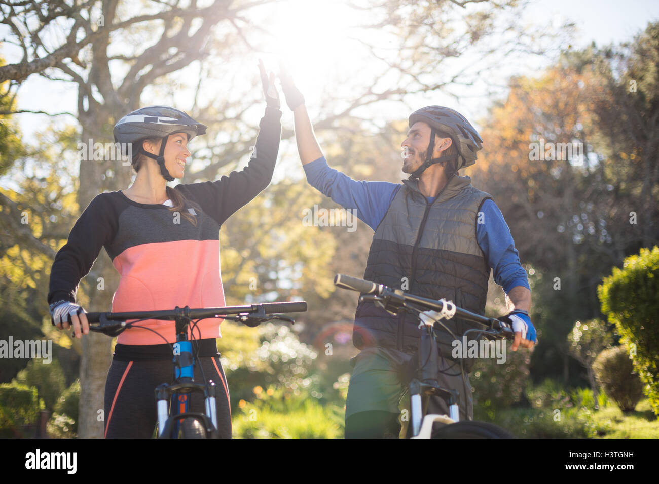 Biker couple giving high five while riding bicycle in countryside Stock ...