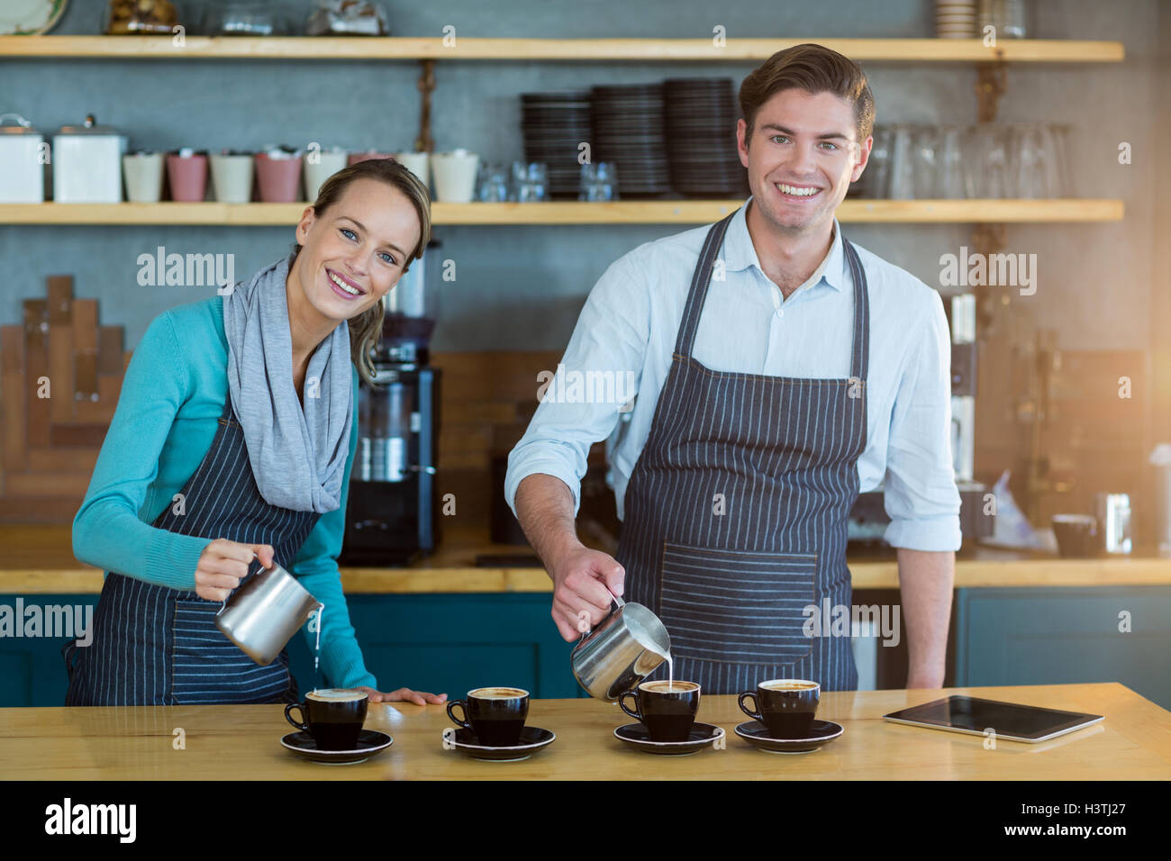 Smiling waiter and waitress making cup of coffee at counter in cafe ...