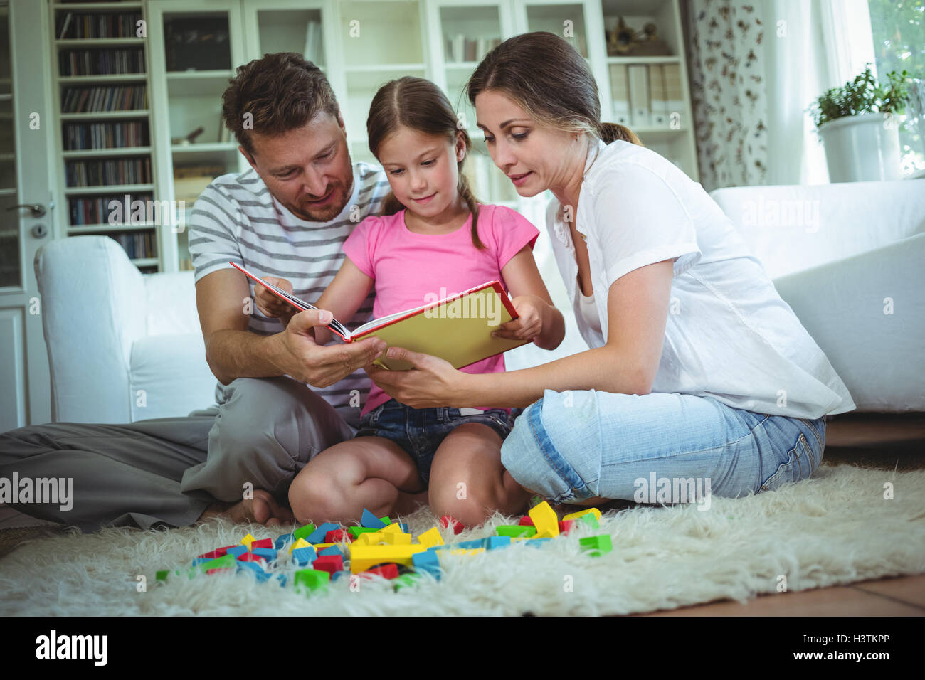 Parents and daughter reading a book while playing with building blocks ...