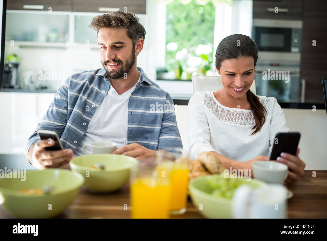 Couple using mobile phone while having breakfast Stock Photo - Alamy