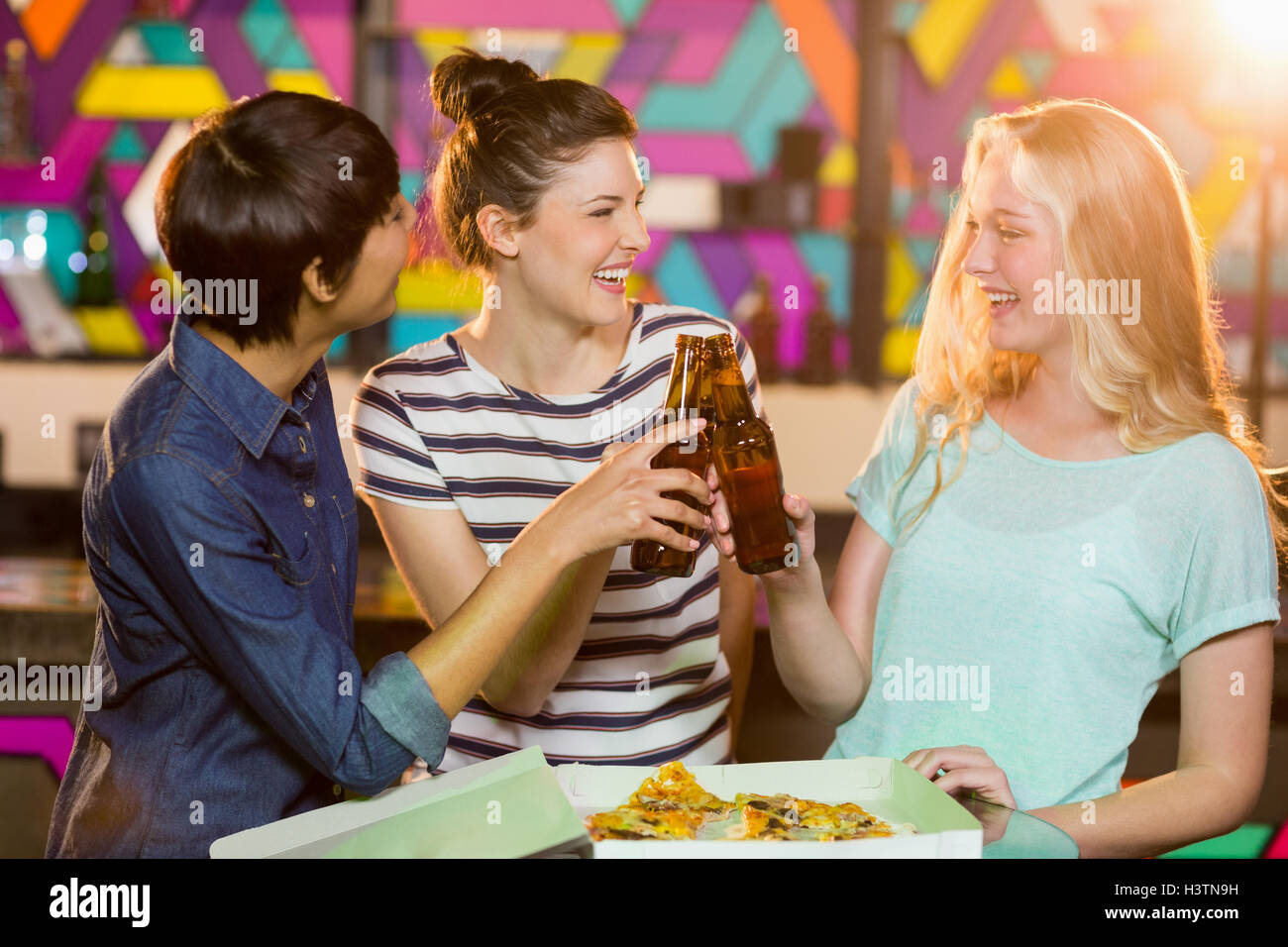 Three female friends toasting bottle of beer Stock Photo - Alamy