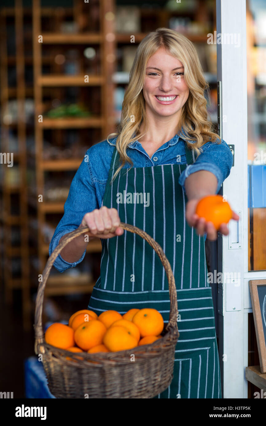 Smiling female staff holding basket of fruit in organic section Stock ...
