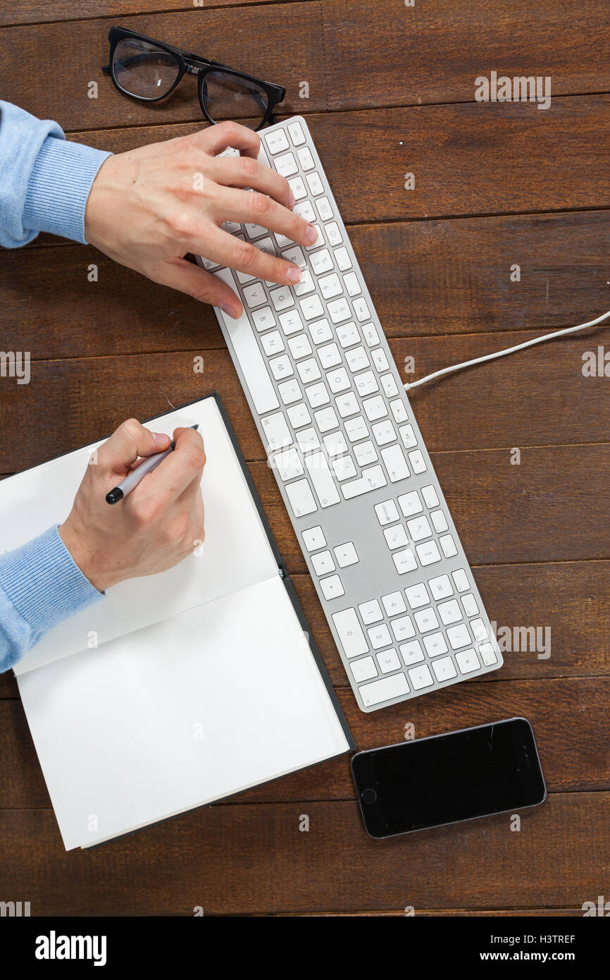 Man typing on keyboard and writing in diary Stock Photo - Alamy