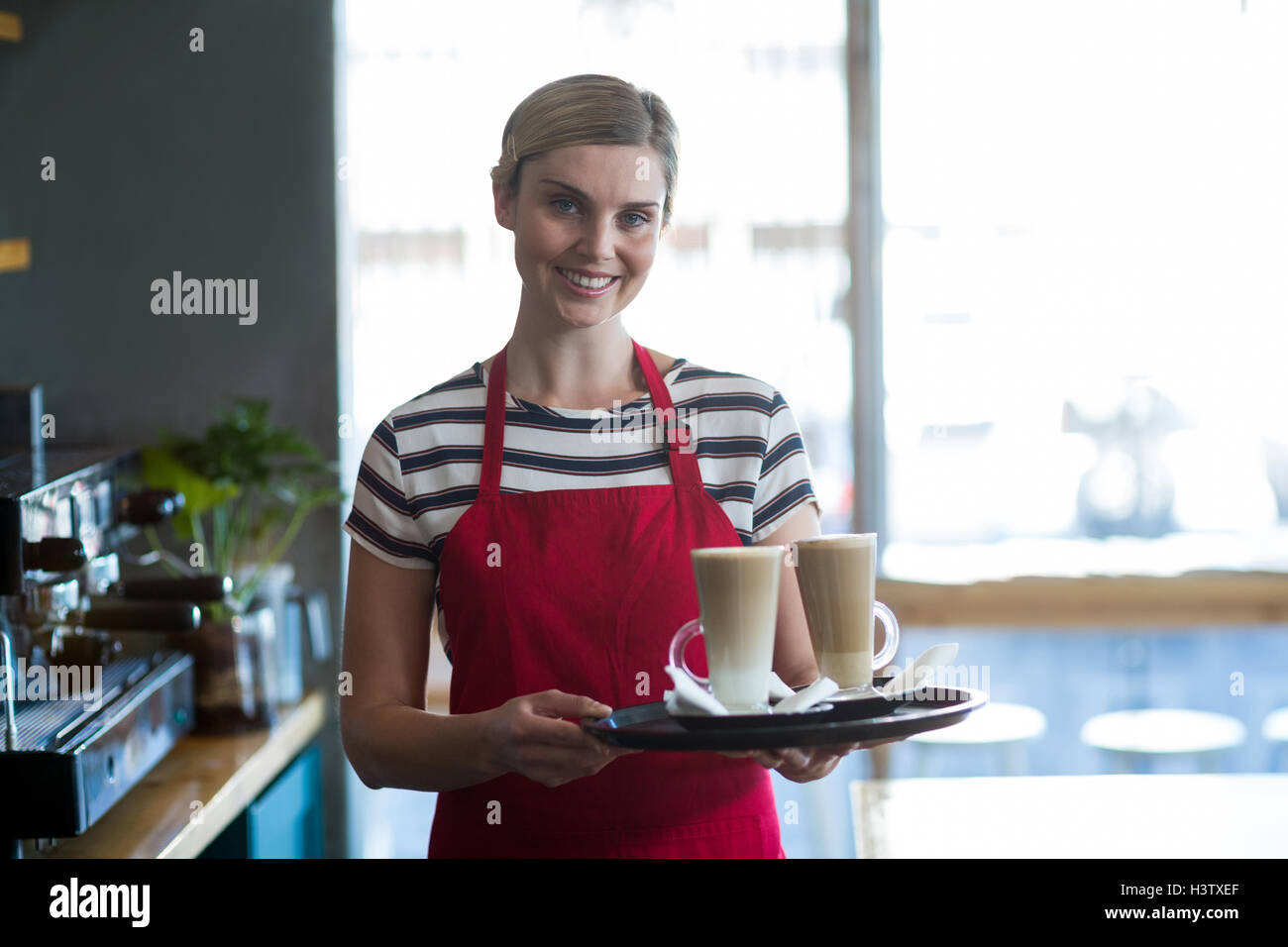 Smiling waitress holding cup of cold coffee at counter in cafe Stock ...