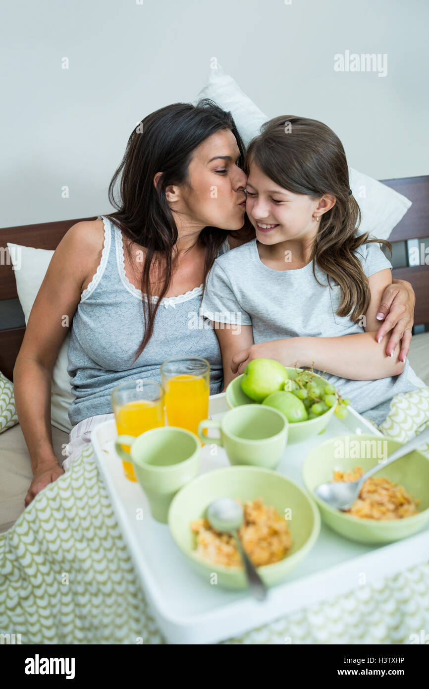 Mother kissing on daughter cheeks while having breakfast on bed Stock ...