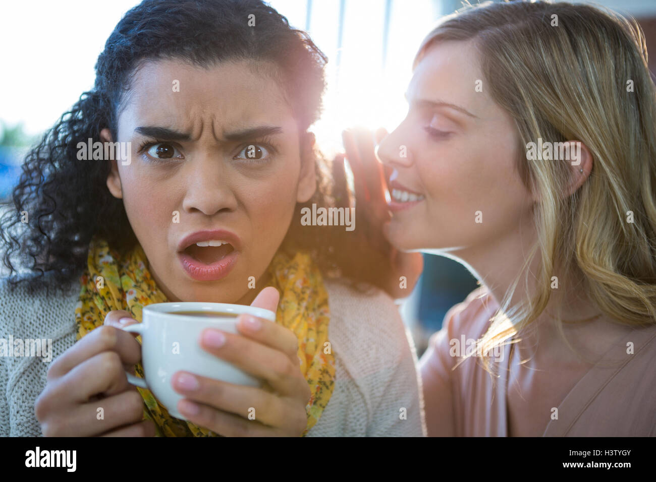 Woman whispering a secret into her friends ear while having coffee ...