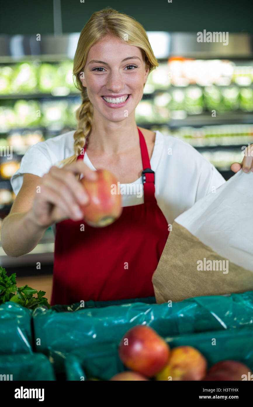 Smiling female staff packing fruits in paper bag at supermarket Stock ...
