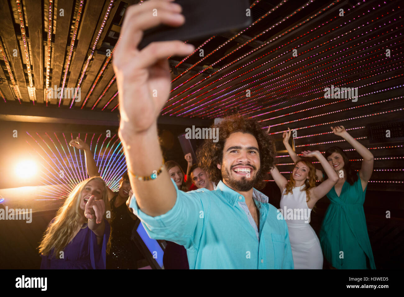 Man taking a selfie from mobile phone while friends dancing on dance ...