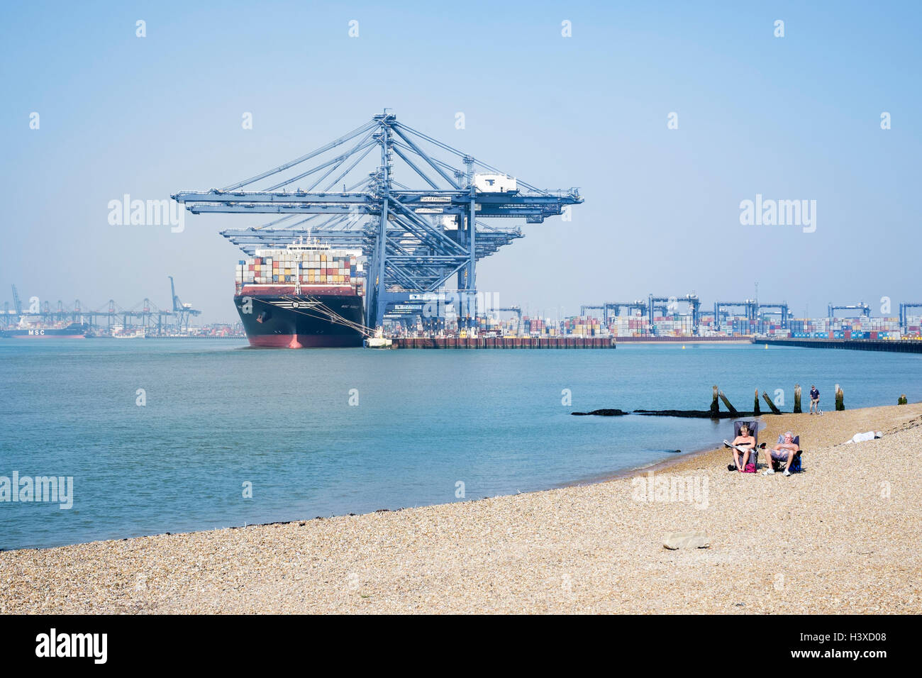 Sunbathers relax on the beach. MSC Venice container ship anchored in ...