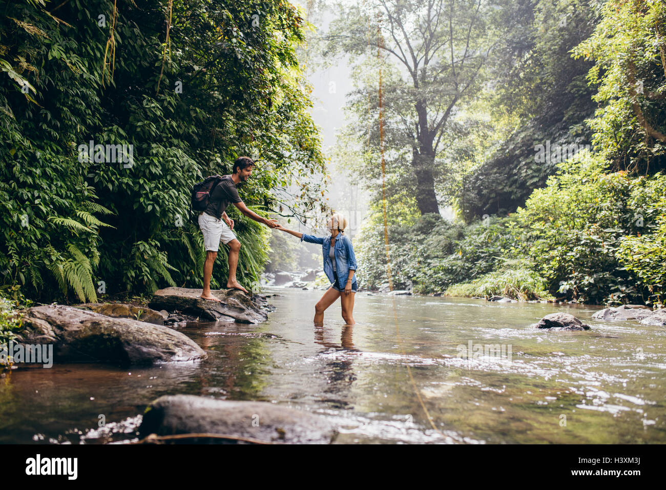 Young couple walking across stream, while man helping woman. Man and ...