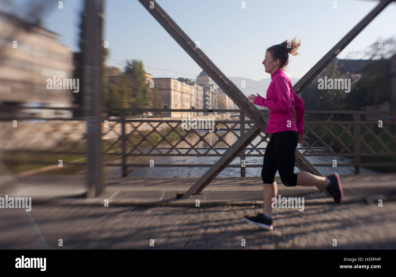 sporty woman running on sidewalk at early morning jogging with city ...
