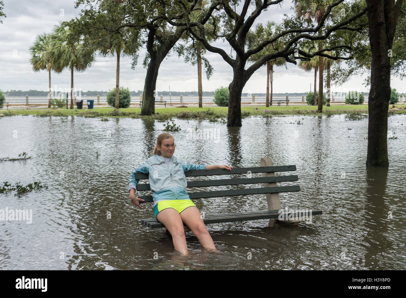 A young girl sits on a park bench surrounded by flood water in White ...