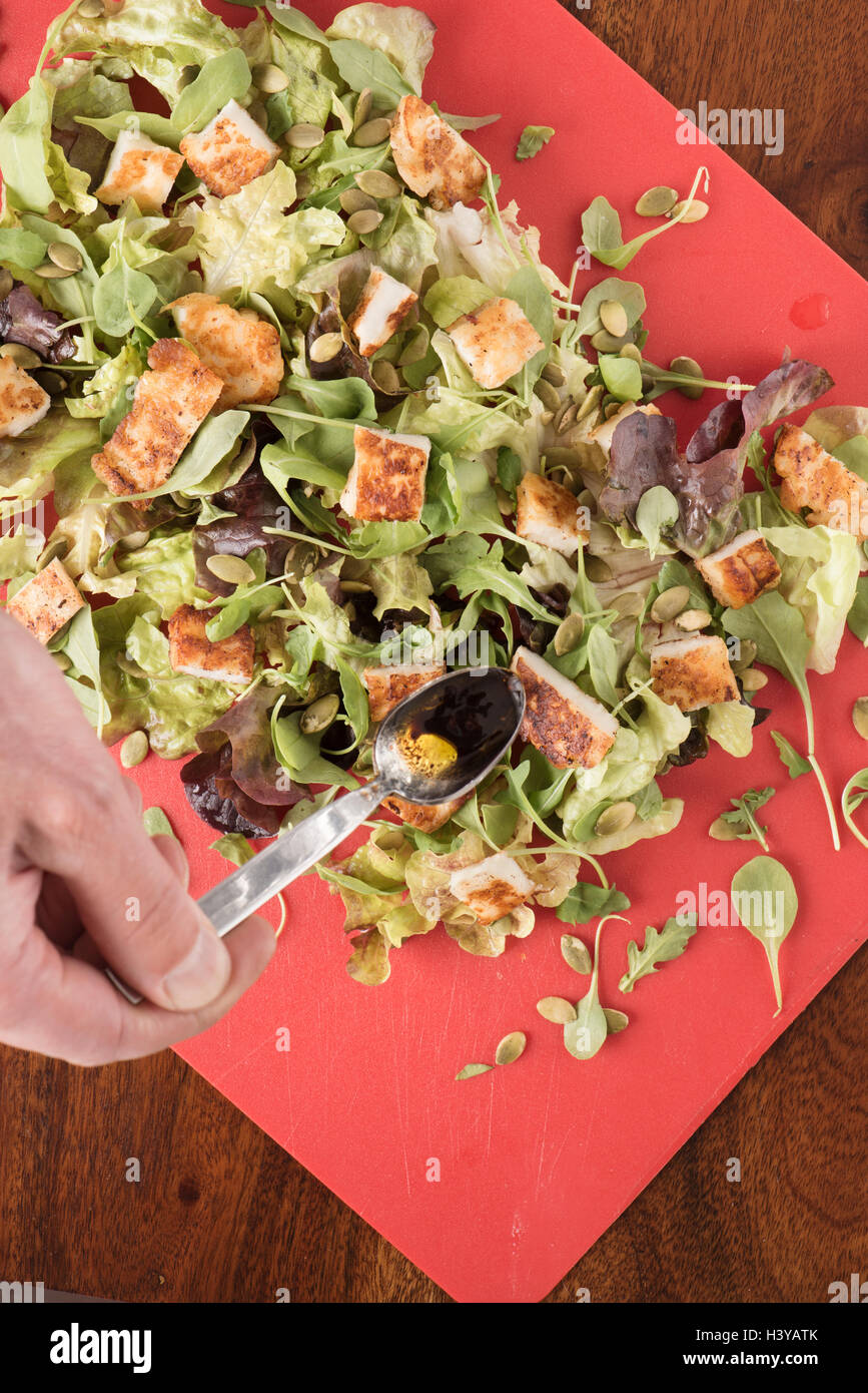 Salad with halloumi cheese being prepared. Chef pouring dressing from ...