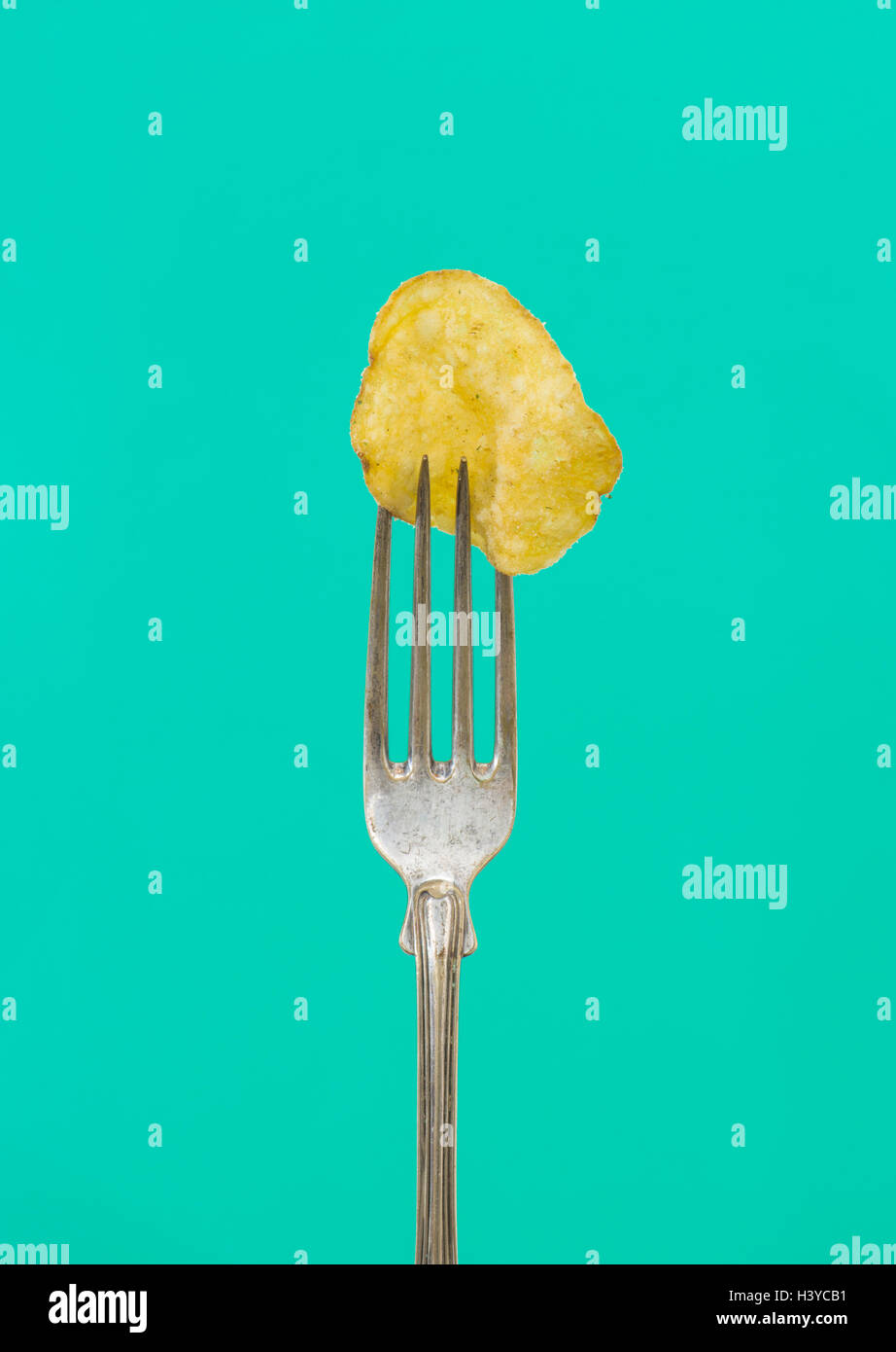 One potato chip on fork. Close up of salty and fat snack. Concept of ...